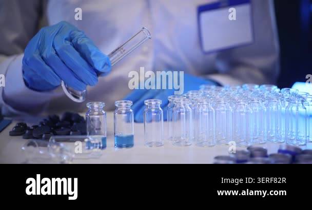 Experienced laboratory employee fills tiny glass vials with blue ...