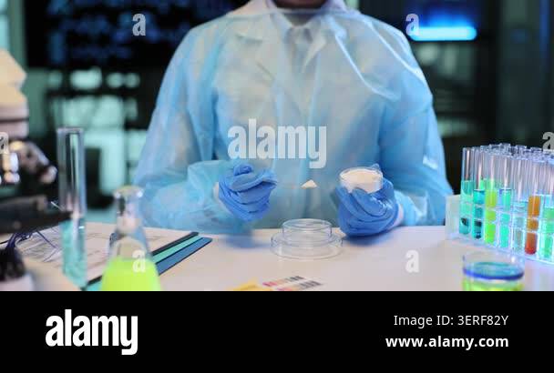 Chemist wearing full protective clothing carefully examines white ...