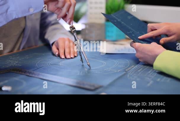 Woman designer draws circle with compass on blueprint as colleague ...