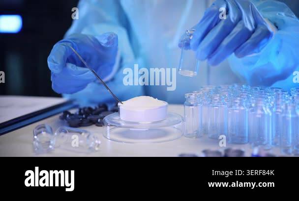 Lab technician transfers soft white powder into miniature glass ...