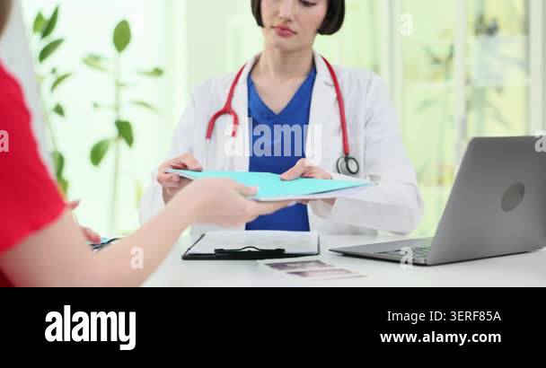 Woman doctor accepts medical folder from patient at clinic desk ...