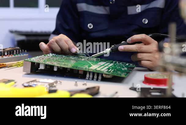 Close-up of a technician soldering a green circuit board at a workbench ...