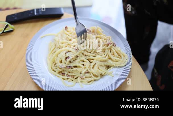 Hungry man carefully twirls creamy carbonara around silver fork at ...