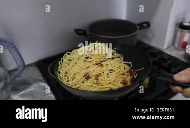 Chef mixes tender spaghetti with crispy bacon by shaking heavy black ...