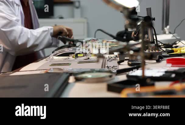 Technician in a lab coat repairs an electronic circuit board at a ...