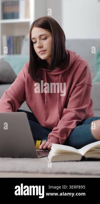 Woman studies on laptop at home in a cozy setting with books around her ...