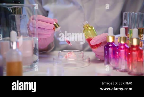 Pharmacist drips essential oil onto cream in glass Petri dish in ...