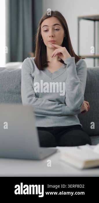 Woman sits at home, focused on laptop with different expressions and ...