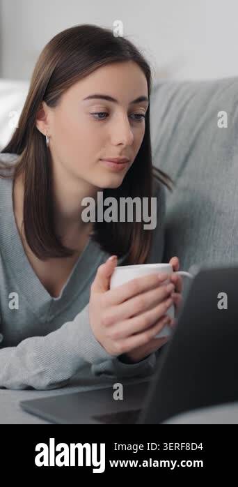 Woman sits with a laptop and cup at home, focusing on work and enjoying ...