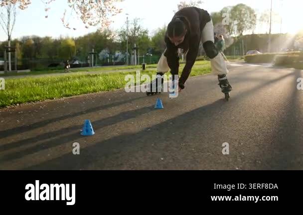A young woman on inline skates places blue cones on a paved path in a ...