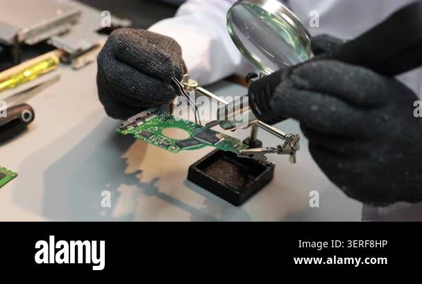 Technician in protective gloves repairs a green circuit board with a ...