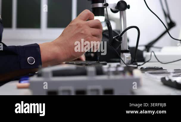 Close up of a technician repairing a small electronic device under a ...