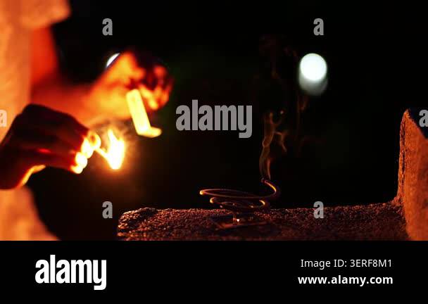 Close up of a human hand using a burning match to light a spiral ...