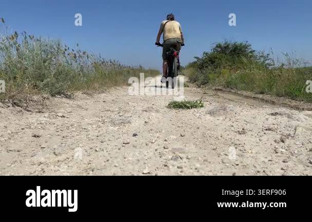 Ground-level view of a mountain biker riding along a stony dirt track ...