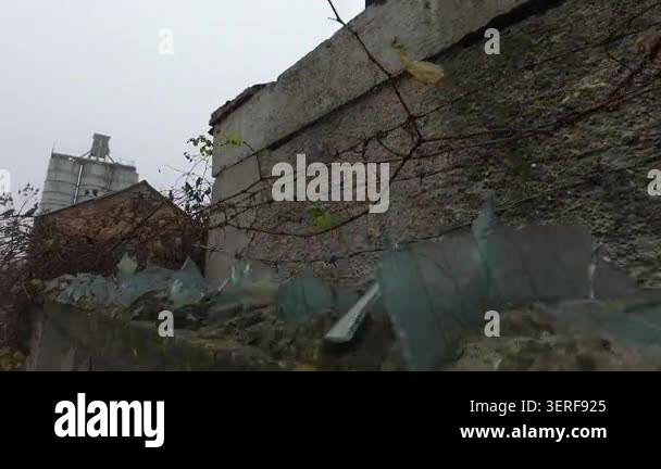 Broken glass and rusty barbed wire top the weathered concrete wall of ...