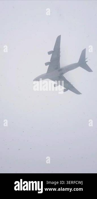 Aircraft flying through snowy winter sky during adverse weather ...