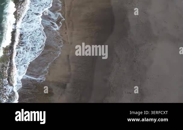 Aerial view of ocean waves crashing on a sandy beach, showcasing the ...