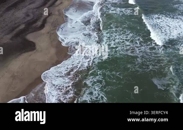 Aerial view of ocean waves crashing on a sandy beach, showcasing the ...