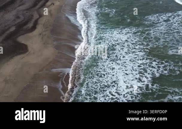 Aerial view of ocean waves crashing on a sandy beach, showing the ...