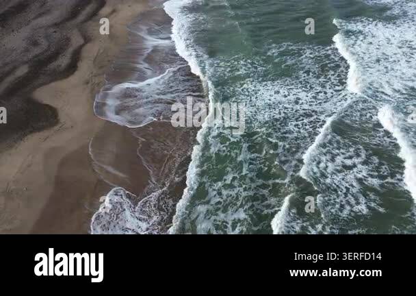 Aerial view of ocean waves crashing on a sandy beach, showcasing the ...