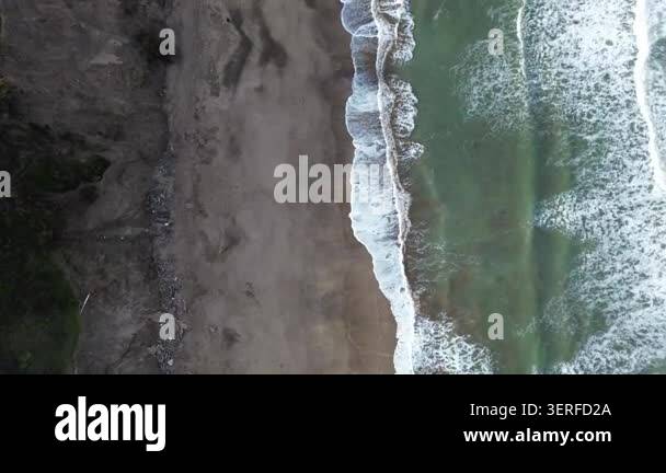 Aerial view of ocean waves crashing on a sandy beach with a cliffside ...