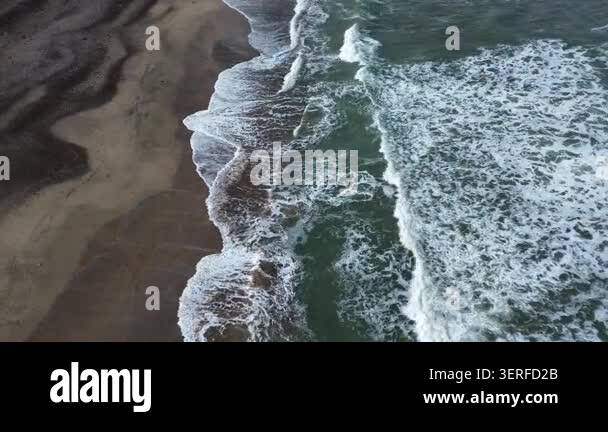 Aerial view of ocean waves crashing on a sandy beach, showcasing the ...