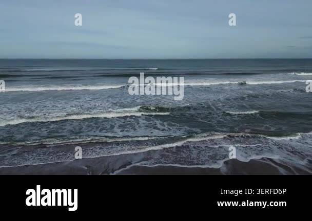 Aerial view of ocean waves crashing on a beach under a cloudy sky ...