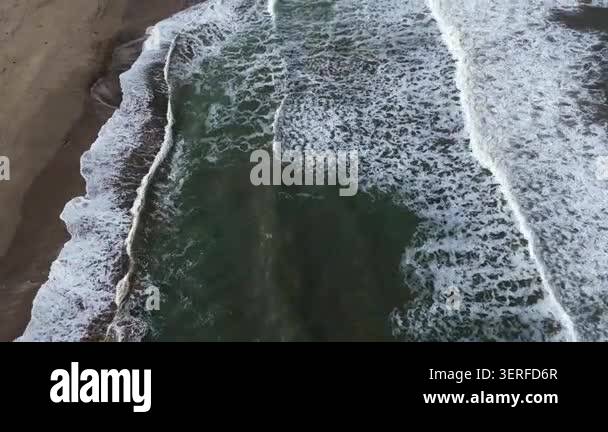 Aerial view of ocean waves crashing on a sandy beach, showing the ...