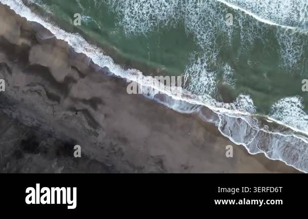 Aerial drone footage of ocean waves crashing on a sandy beach ...