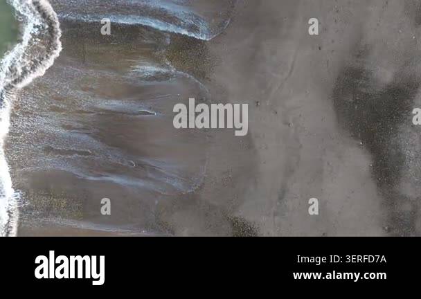 Aerial view of ocean waves crashing on a sandy beach, showcasing the ...