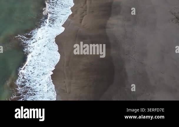 Aerial view of ocean waves crashing on a sandy beach, showcasing the ...