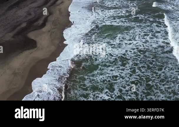 Aerial view of ocean waves crashing on a sandy beach with a lone person ...