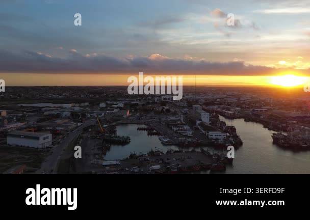 Aerial drone footage captures a coastal city and harbor at sunset with ...