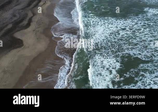 Aerial view of ocean waves crashing on a sandy beach, showcasing the ...