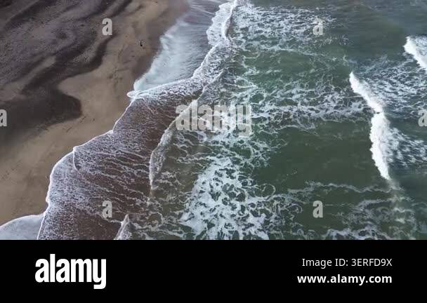 Aerial view of ocean waves crashing on a sandy beach with a lone person ...