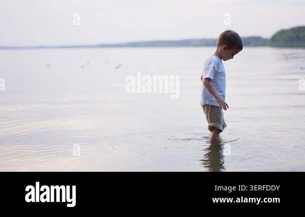 Small boy wading in calm lake water at sunset. Side view of toddler ...