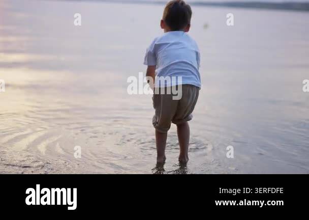 Back view of a boy standing at the water edge at dusk. Rear silhouette ...