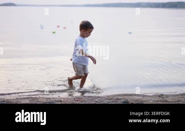 Barefoot child stepping into river water with paper boats floating ...