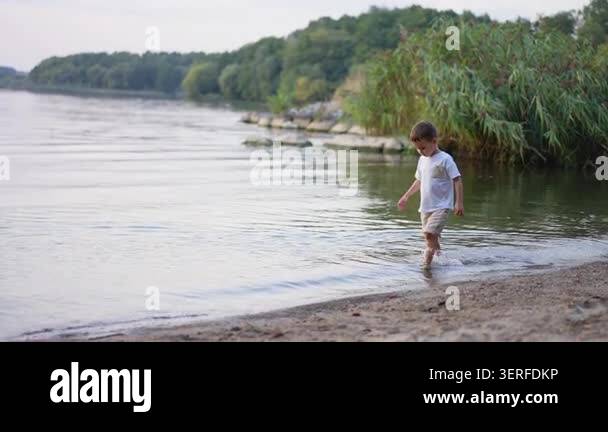 Child wading through shallow water near reeds on a river shore. Side ...