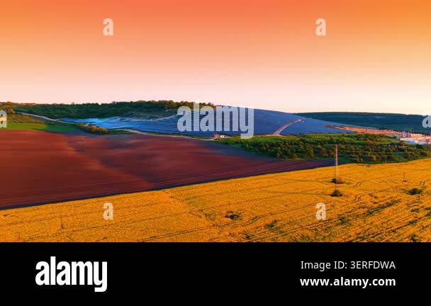 Sunset light over solar farm and golden wheat fields. Warm orange sky ...
