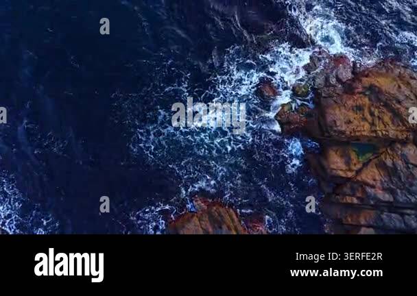 Waves crashing against coastal rocks seen from above. Top down drone ...