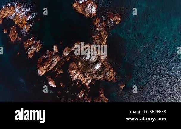Jagged rock formation surrounded by deep teal ocean water. Overhead ...