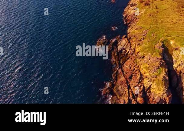 Sunlit rocky coastline edge with deep blue ocean from above. Aerial ...