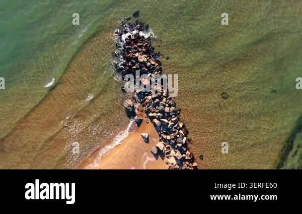 Stone jetty reaching into turquoise water from sandy shoreline ...