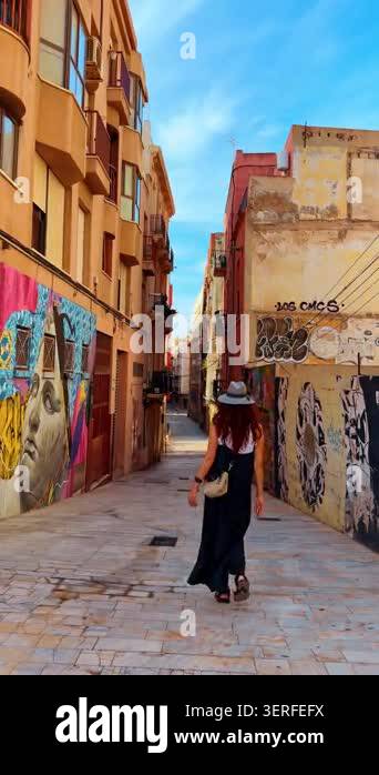 Alicante, Spain, 8 August 2025: Woman exploring graffiti covered alley ...
