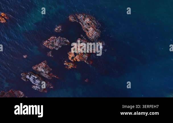 Overhead view of rocky reef in dark blue sea. Layered red and brown ...