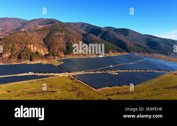 Fenced solar array on green pasture with cattle below mountain ridge ...