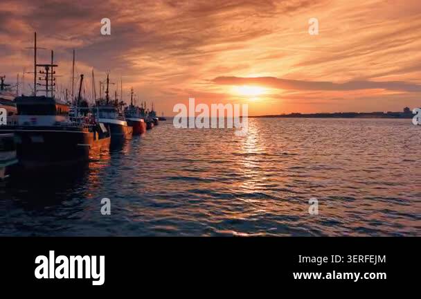 Sunset over fishing boats moored at harbor pier. Warm golden light ...