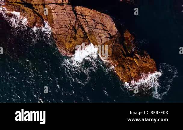 Sunlit rocky cliff with waves crashing from drone perspective ...