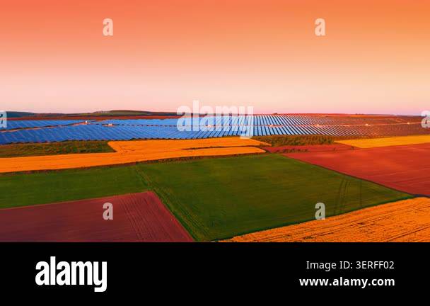 Sunset light casting warm glow on solar farm amid crop fields ...